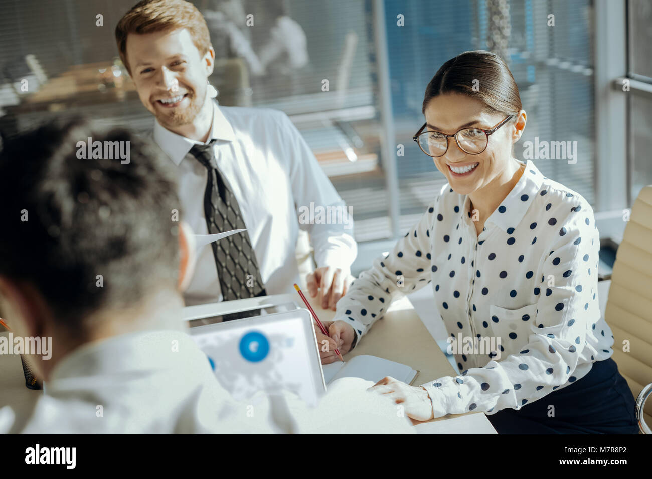 Upbeat office workers smiling while listening to their colleague ...
