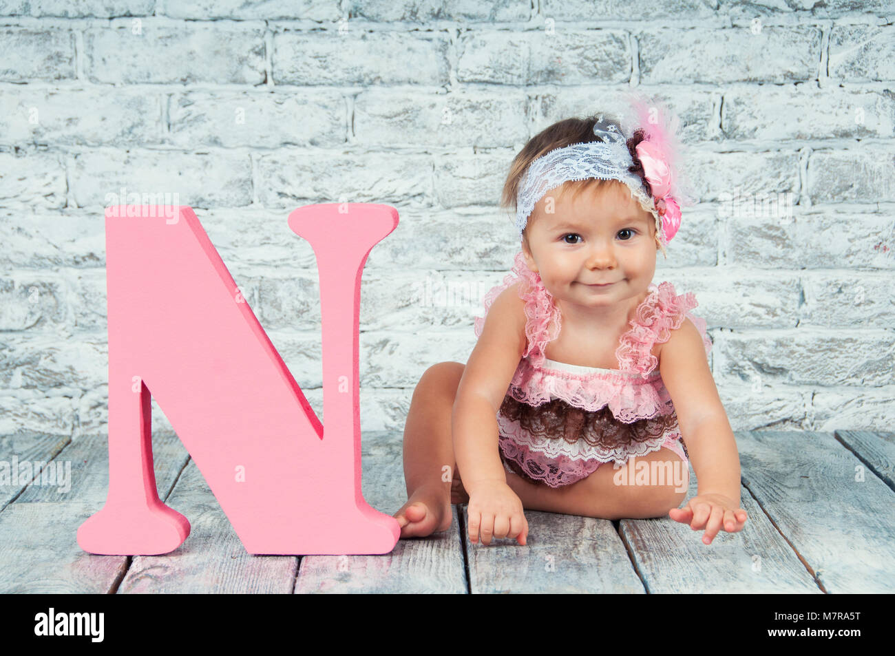 Beautiful and cute girl in pink dress with the letter N. Emotional girl ...