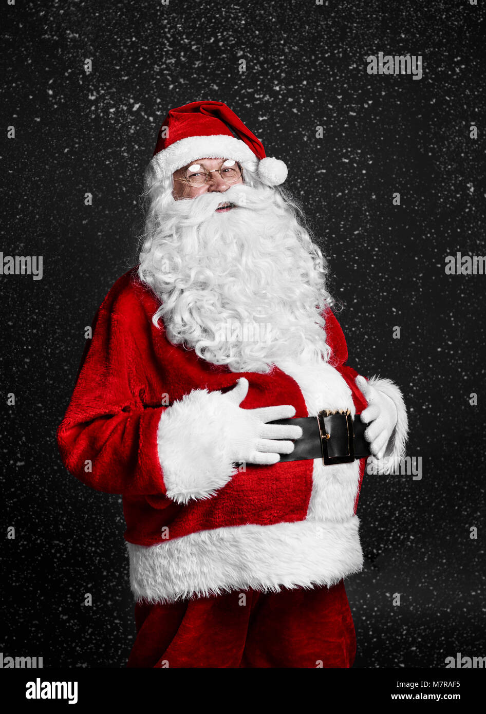 Cheerful santa claus touching his belly among snow falling Stock Photo ...