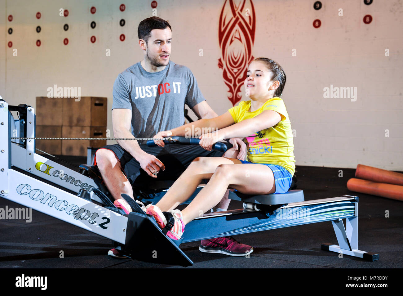 A young girl been given a lesson on a rowing machine in a gym Stock ...