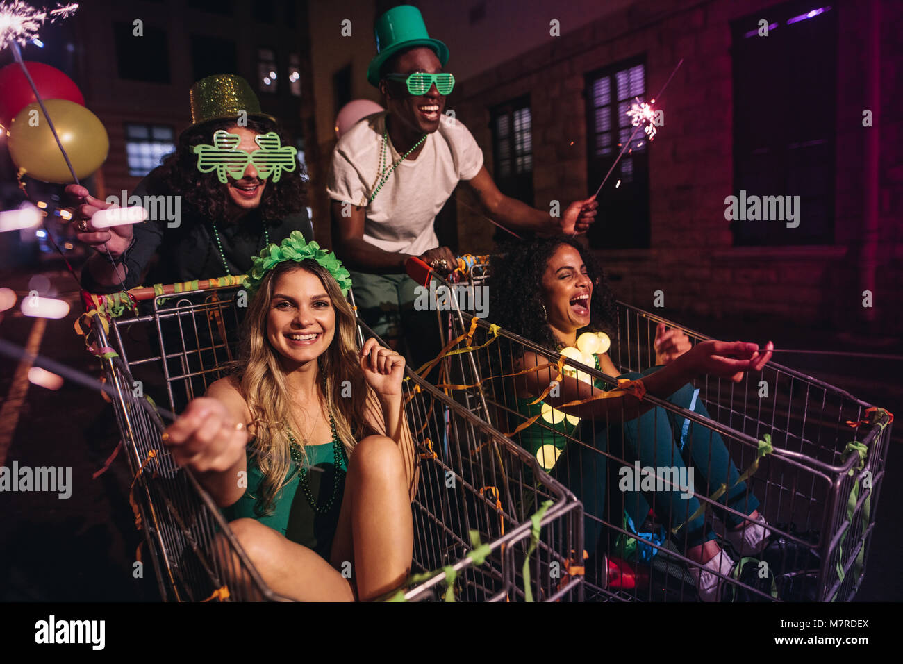 Multiracial young people riding on shopping trolleys on the street with ...