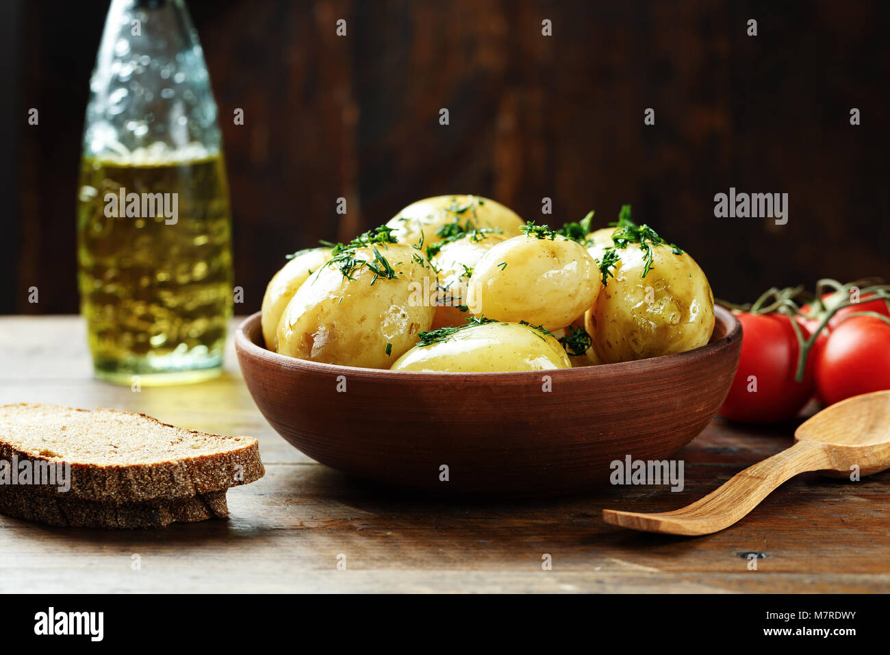 Cooked young potatoes with chopped dill in a clay plate on a wooden ...