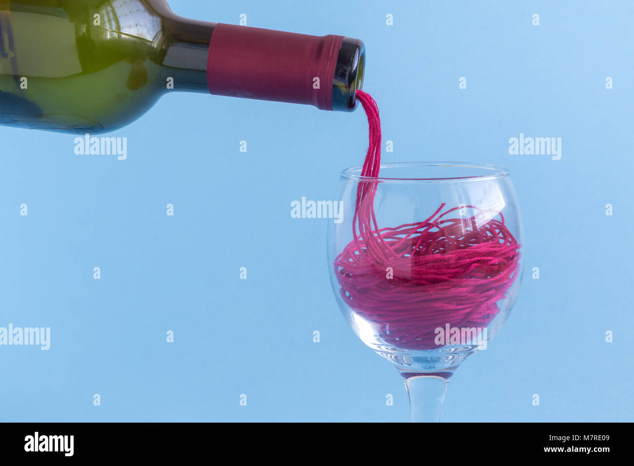 Pouring red wine made of red thread into drinking glass on pastel blue ...