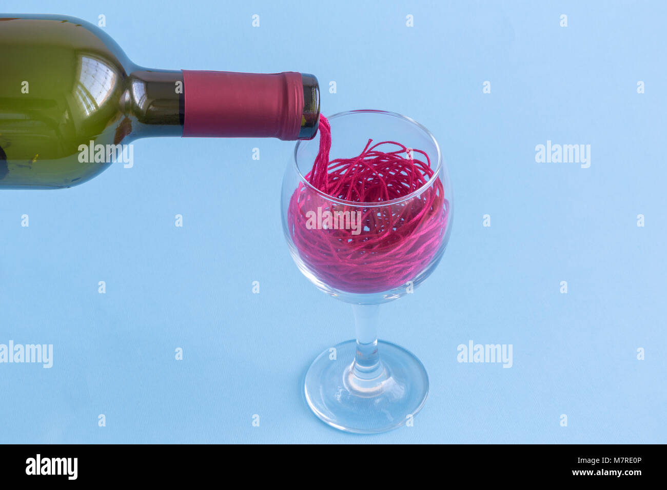 Pouring red wine made of red thread into drinking glass on pastel blue ...