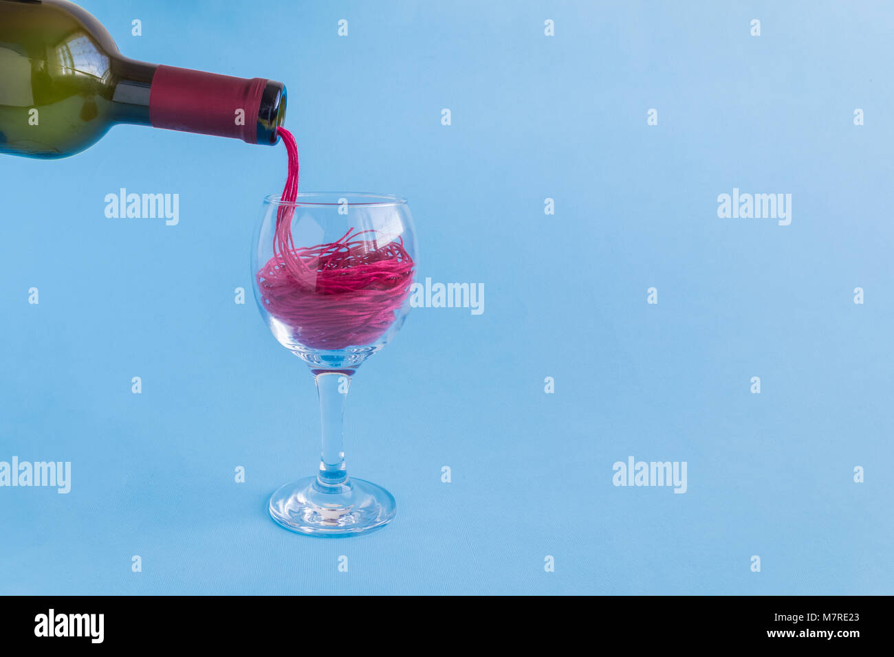 Pouring red wine made of red thread into drinking glass on pastel blue ...