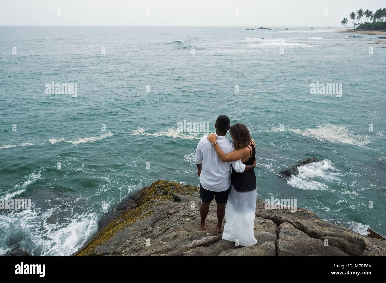 Just married couple on a trstone hugs and looks on the ocean water ...