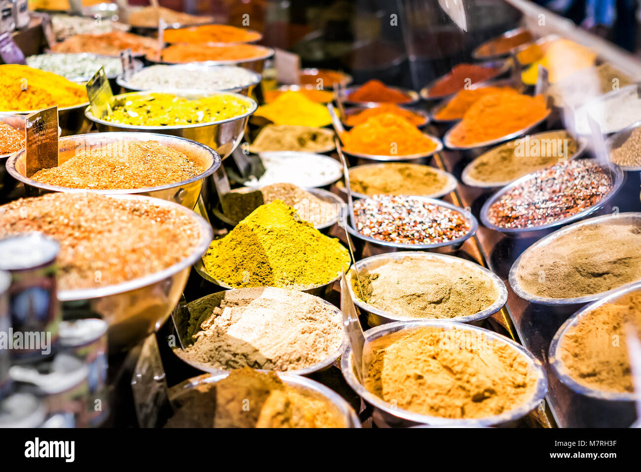 Many spices on display in bowls trays filled with herbs, signs, curry ...