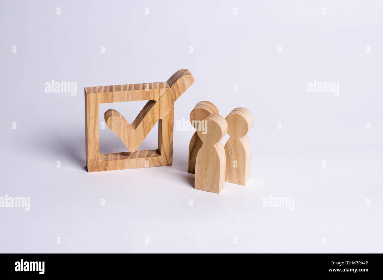Three wooden human figures stand together next to a tick in the box ...