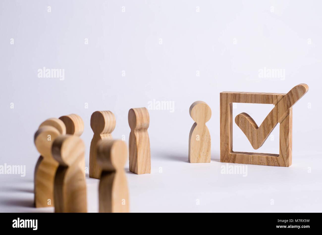 Three wooden human figures stand together next to a tick in the box ...