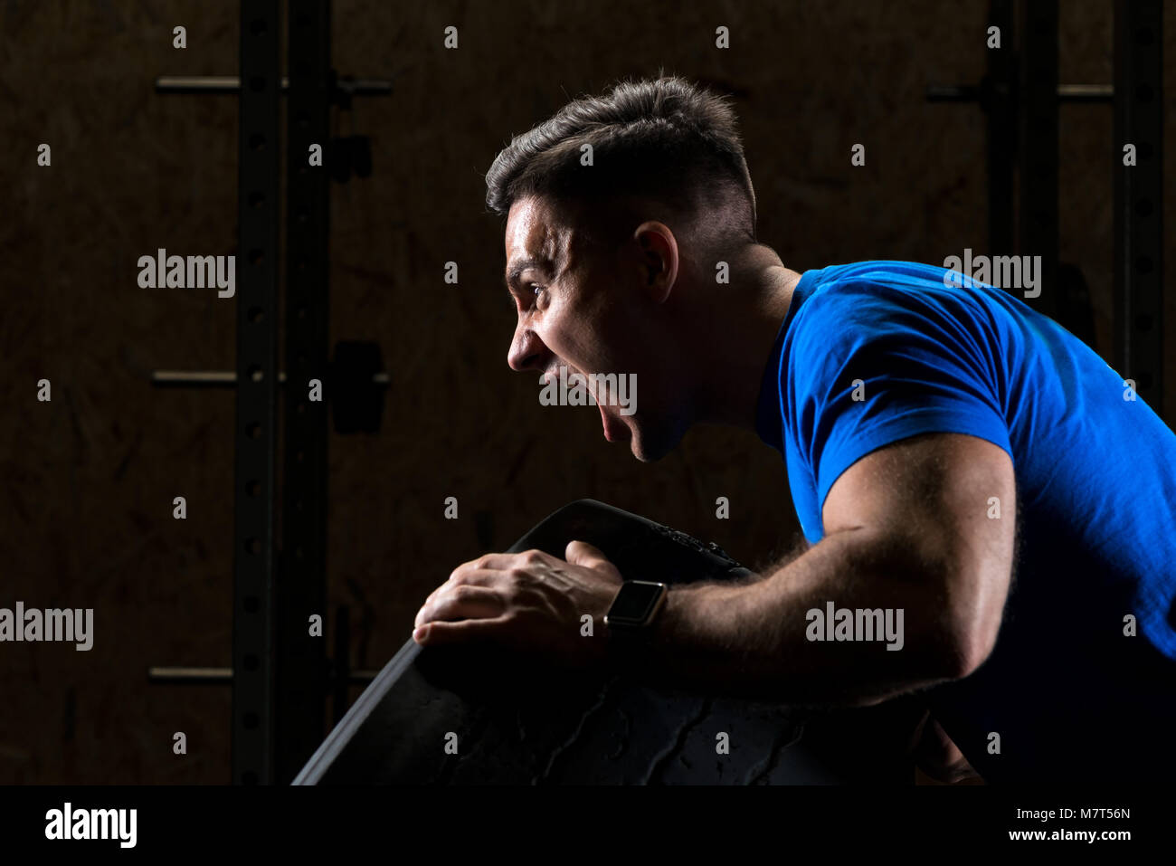 screaming sportsman bodybuilder lifts a heavy heavy wheel, close-up ...