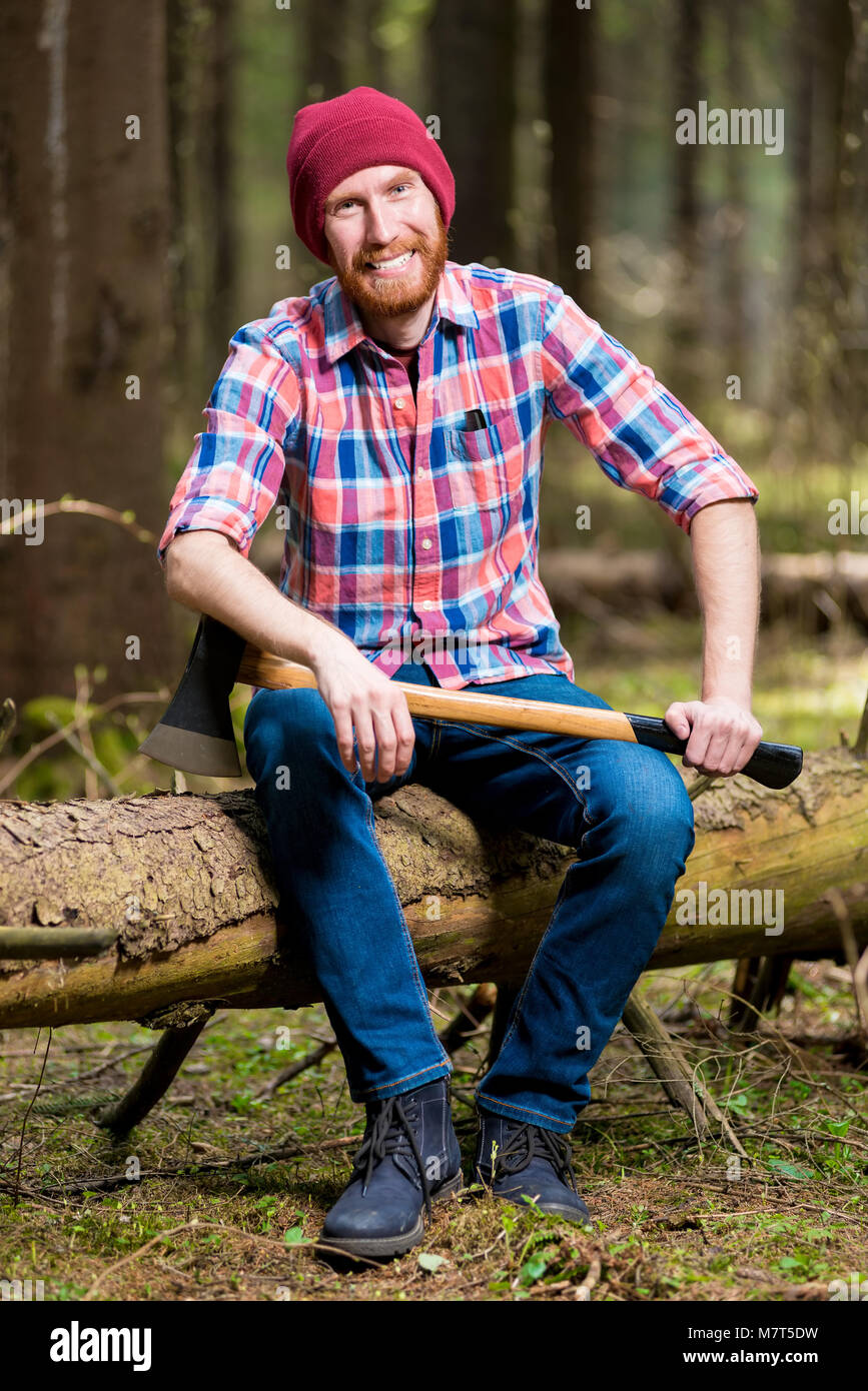 a smiling bearded lumberjack in a hat and shirt with an ax sits on a ...