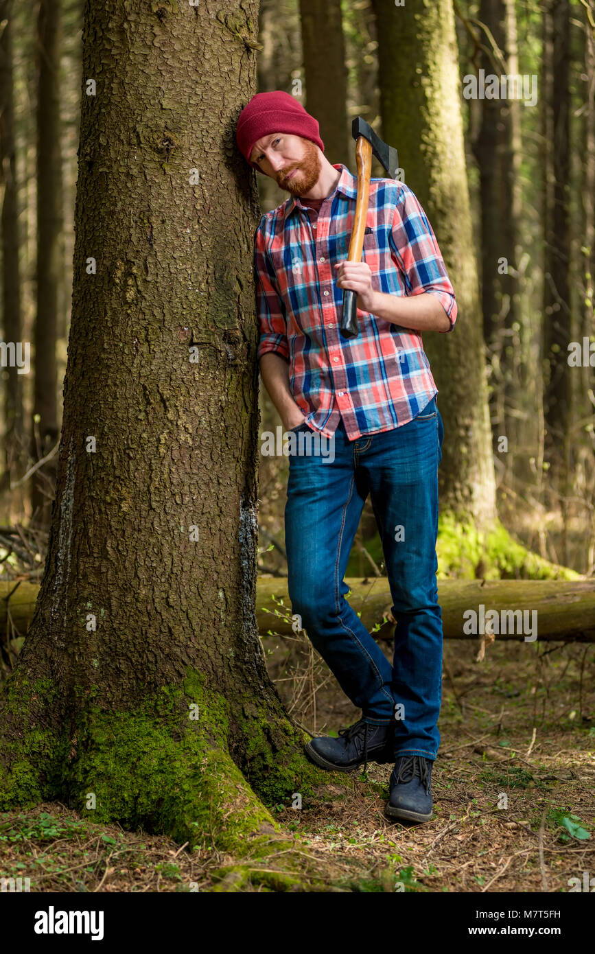 tired bearded lumberjack with an ax resting, leaning against a tree ...