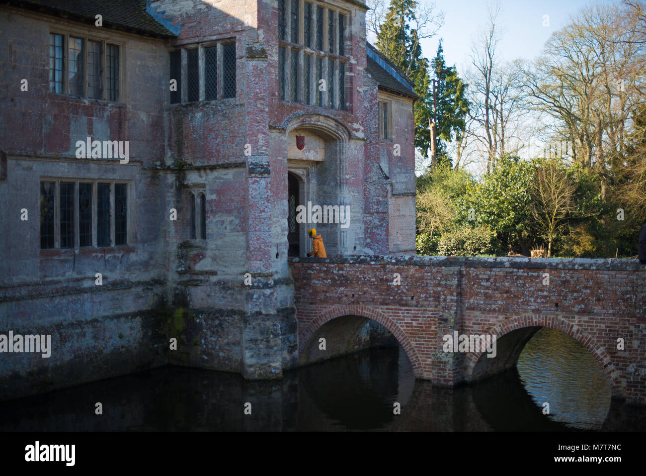 tourist wearing orange crosses arched bridge over moat to enter house ...