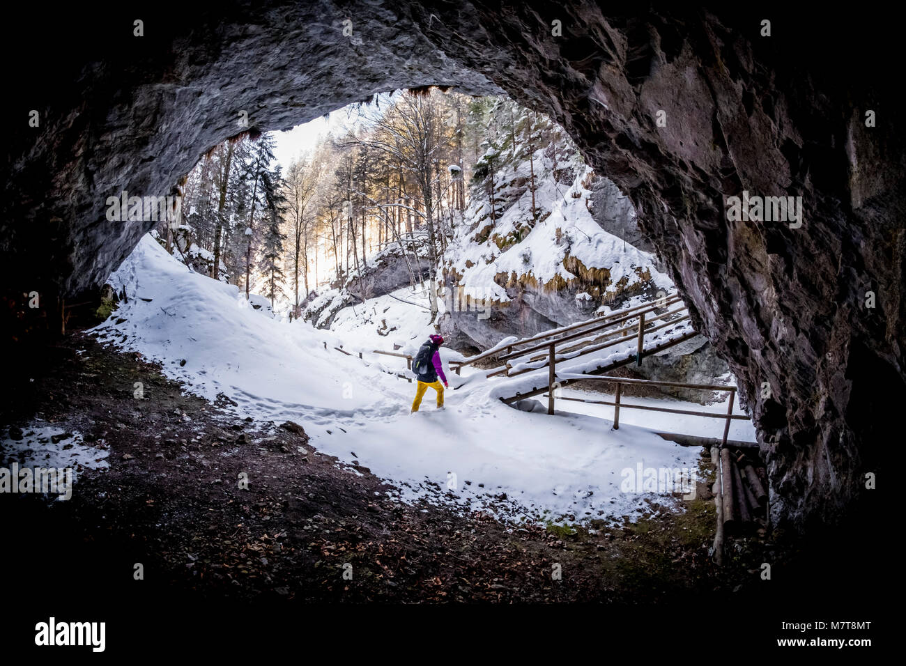 Young women hiking through deep snow from cave to wooden bridge in ...