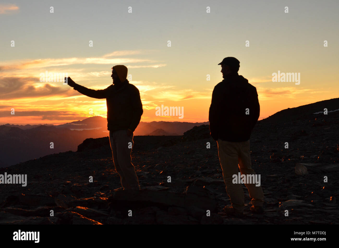 two friends in backlit taking a selfie. Mountain scene during sunset ...