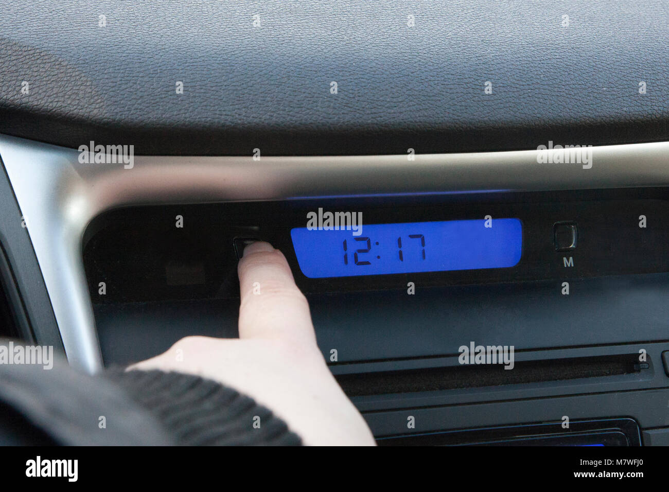 a hand pushes the hour button on a car clock to change the time Stock ...