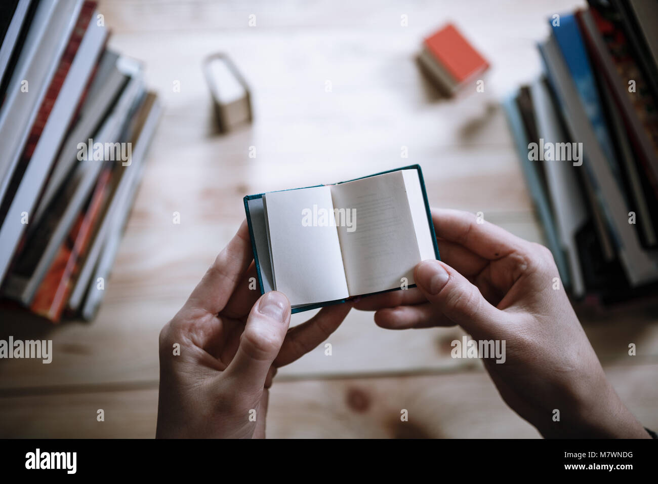 A man reading a miniature book among the big books in the library Stock ...