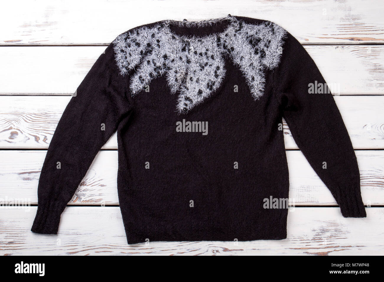 Decorated black sweater. Flat lay, top view. White wooden desk ...