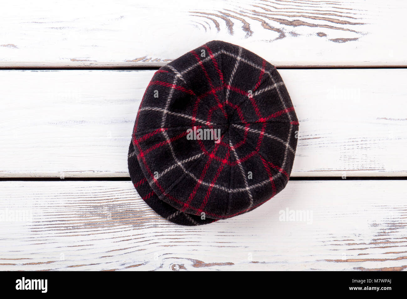 Dark checkered woolen hat. Flat lay, top view. White wooden background ...