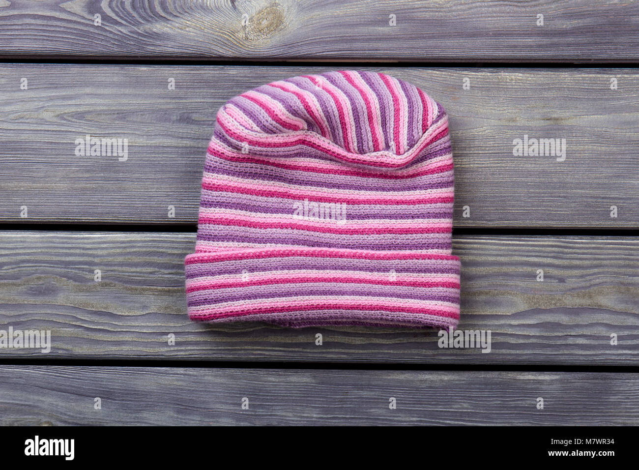 Pink woolen striped hat. Flat lay, top view. Dark wooden desk surface ...