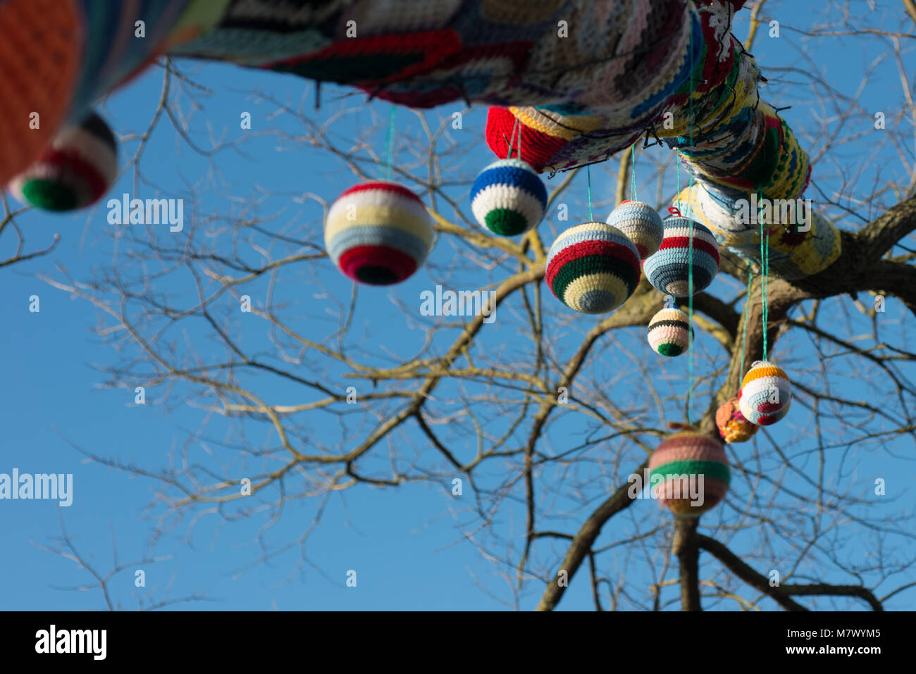 yarn bomb tree with baubles in the winter with blue sky background ...