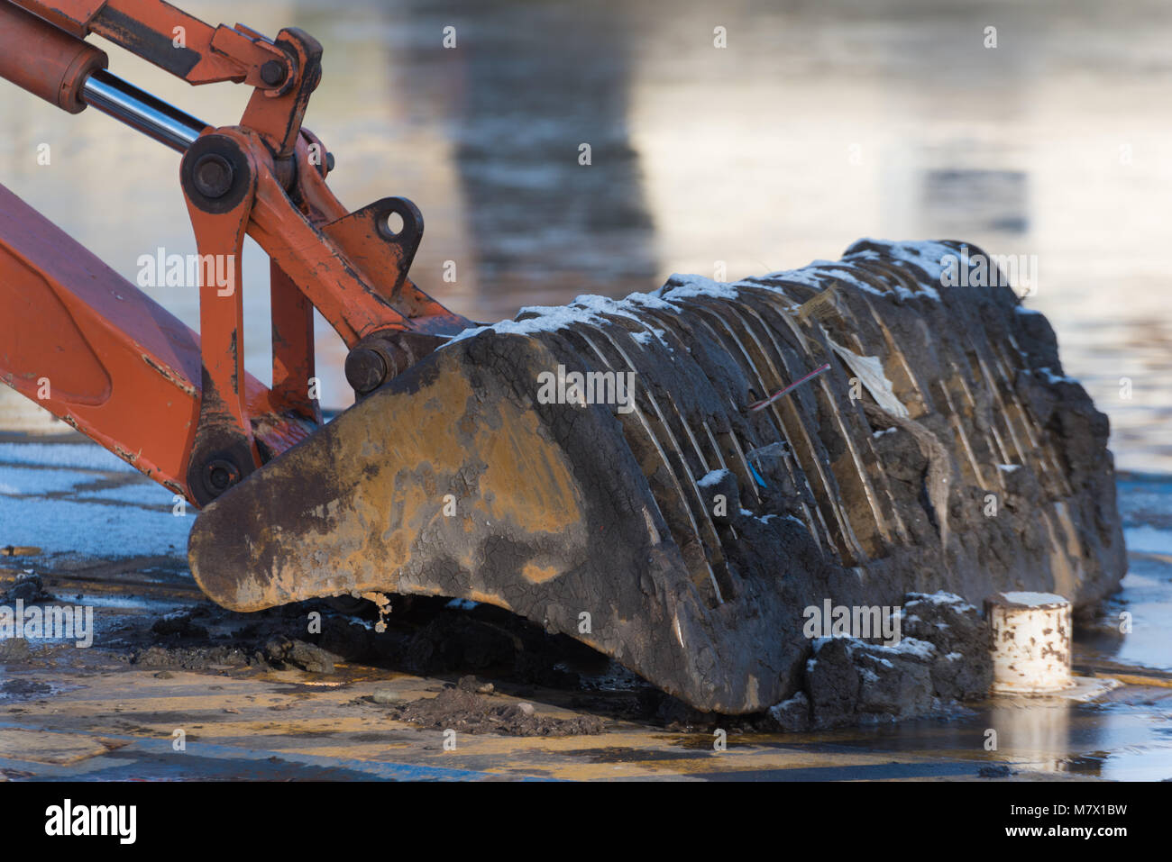 orange excavator digger bucket covered in mud with river water in ...
