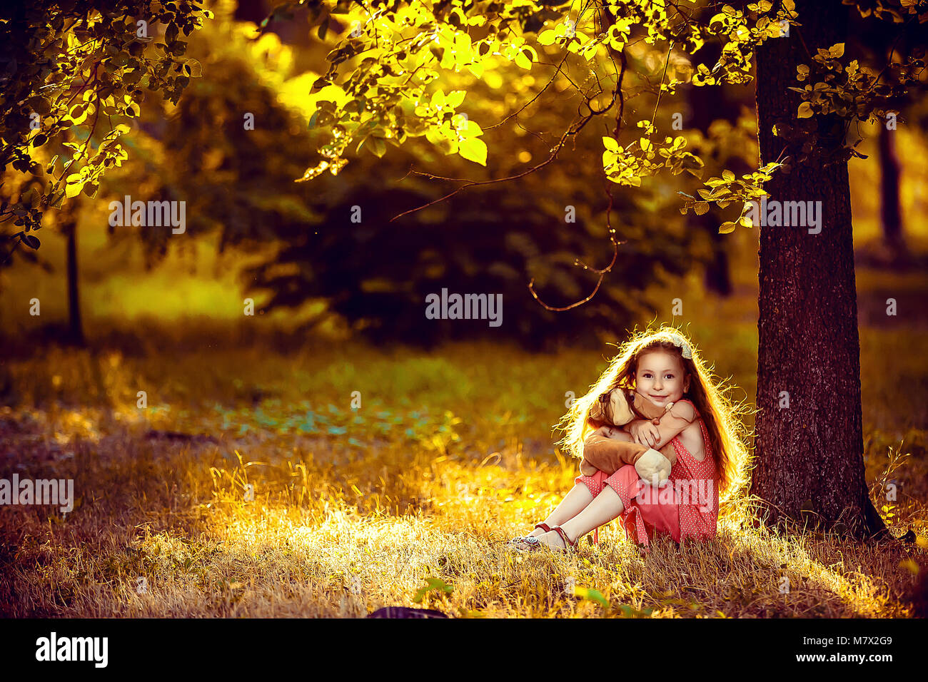 little blonde girl sitting under a birch tree with a toy Stock Photo ...