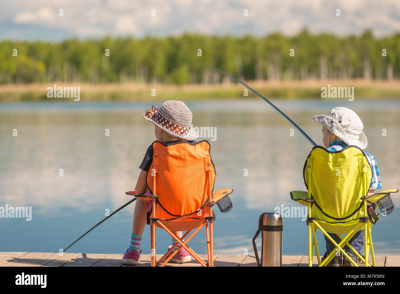 children with fishing rods sit on a wooden pier and fish at the lake ...