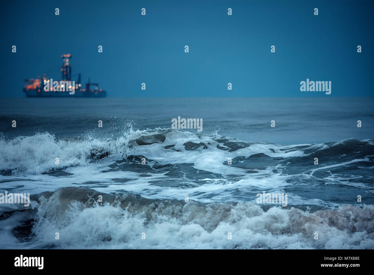 Surfer catches huge waves in the deep sea water after sunset. Cargo ...