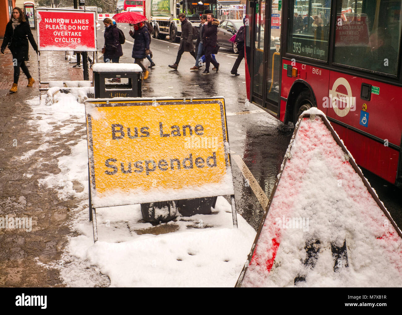 bus lane suspended sign with commuters and red bus in snow storm London ...