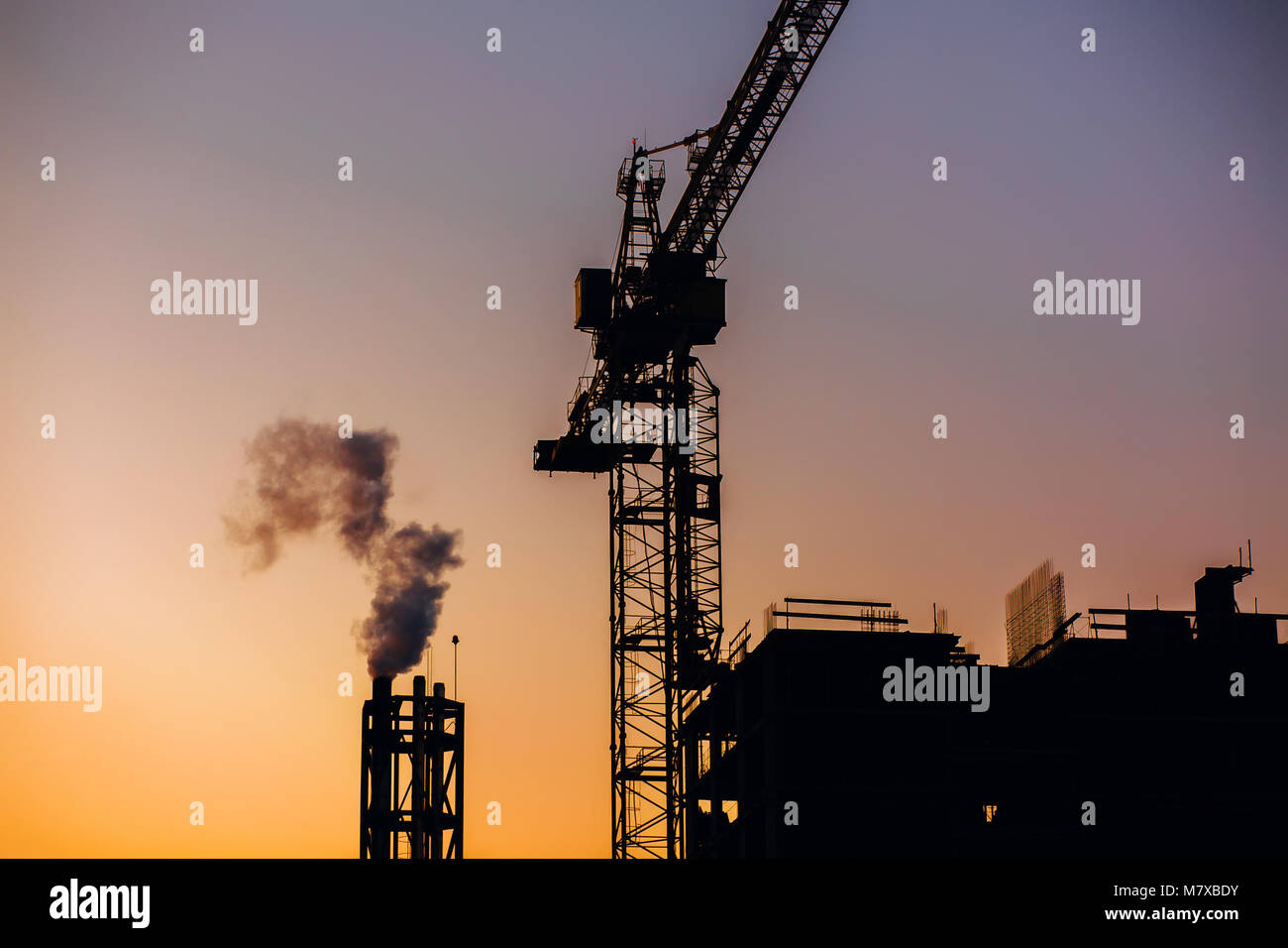 Crane and building construction site with pipe with smoke on background ...
