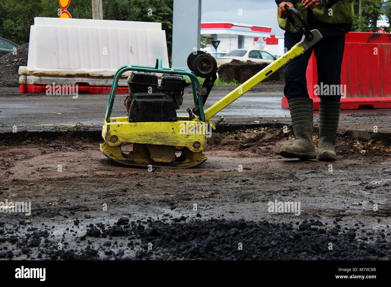 A road construction worker compacts the soil with a compact vibroplate ...
