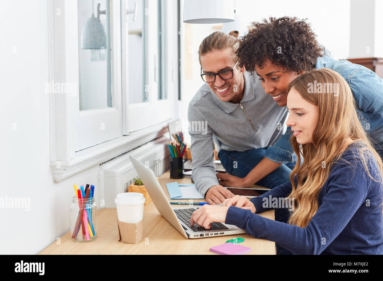 Three students in computer workshop together at laptop in coworking ...