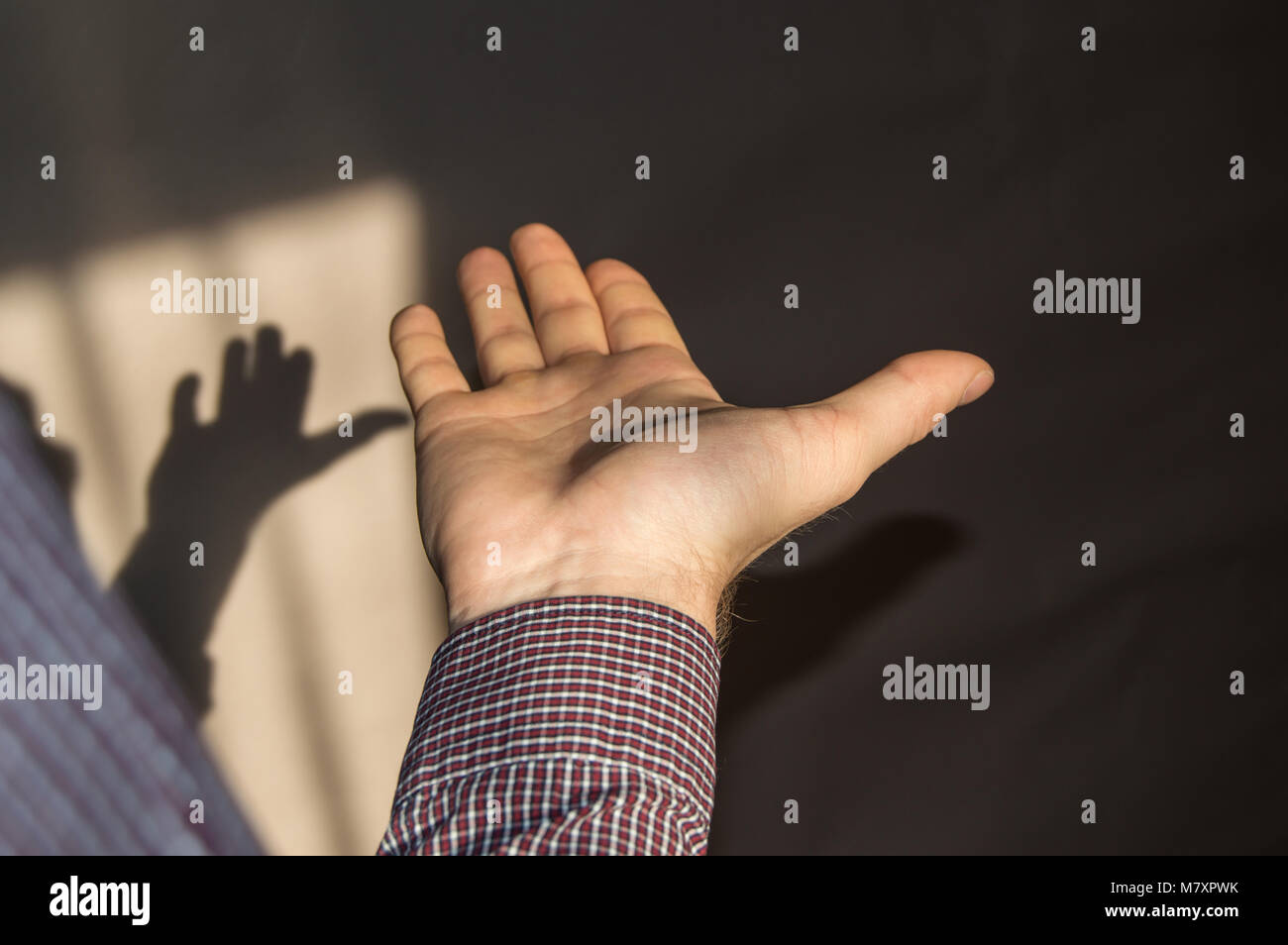 The young man holds an empty hand with his palm up, a shadow on the ...