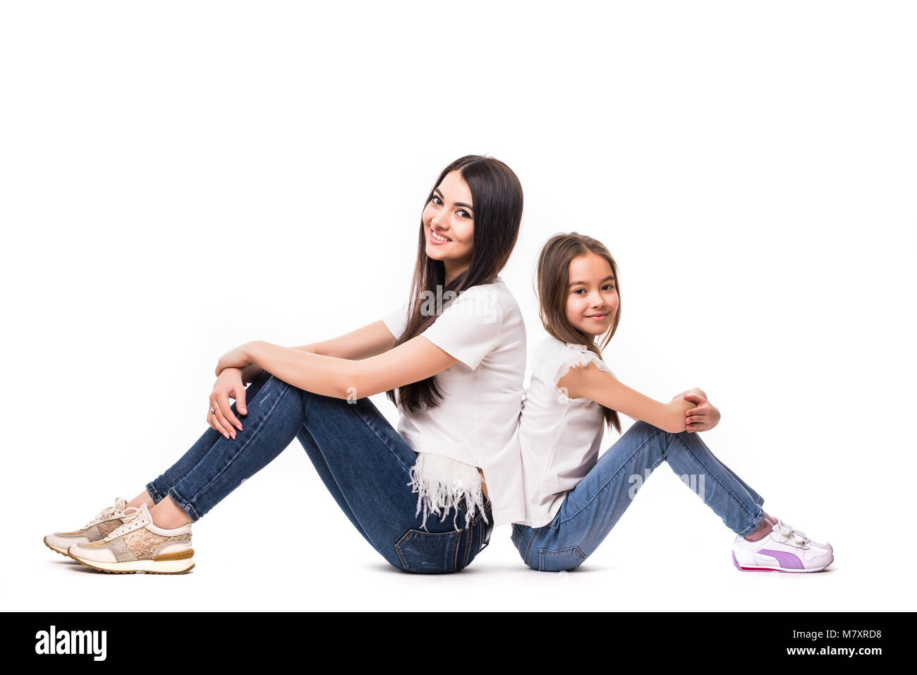 Young little girl and her older sister sitting back to back on white ...