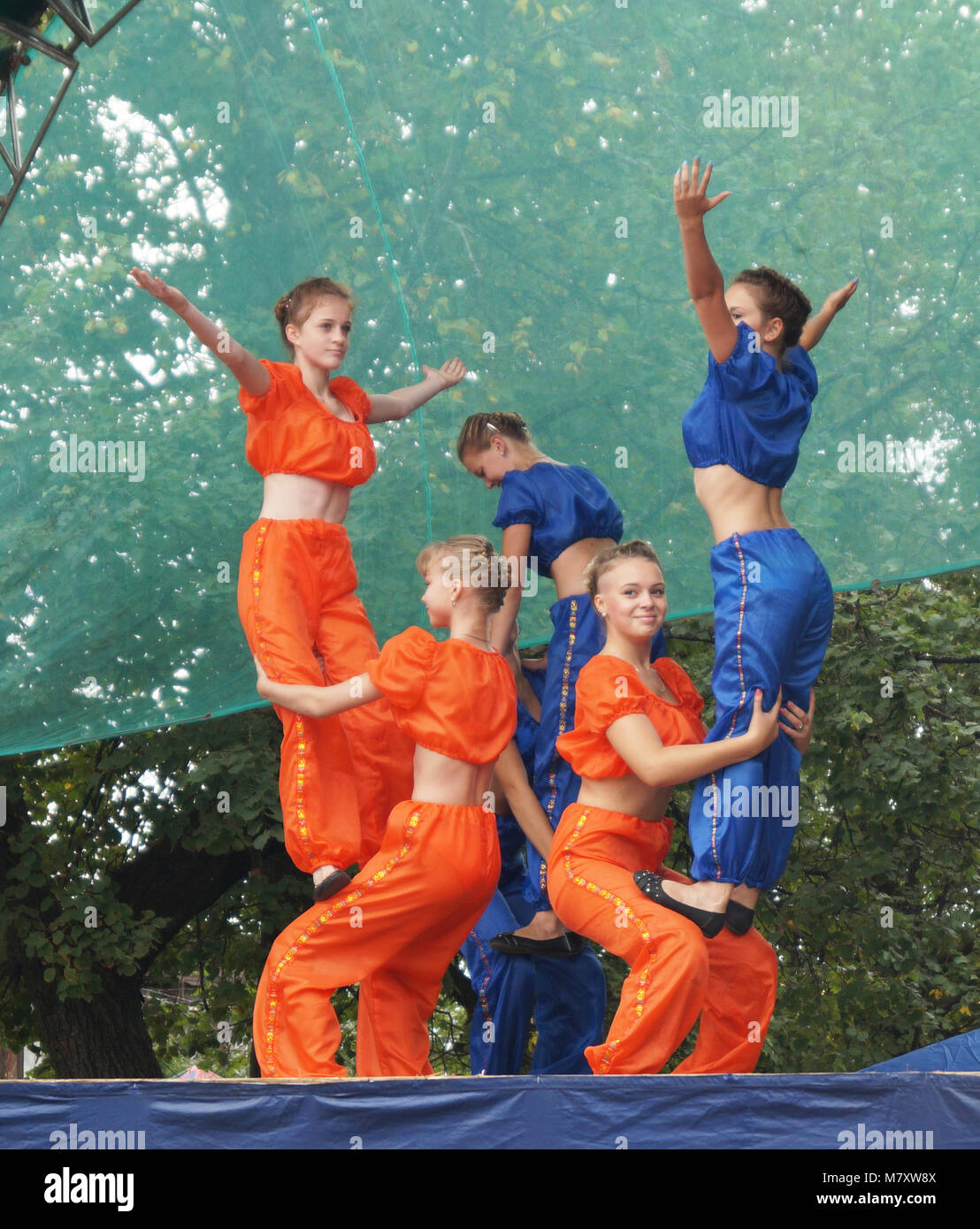 Young girls in bright suit dance and show acrobatic stunts on scene ...