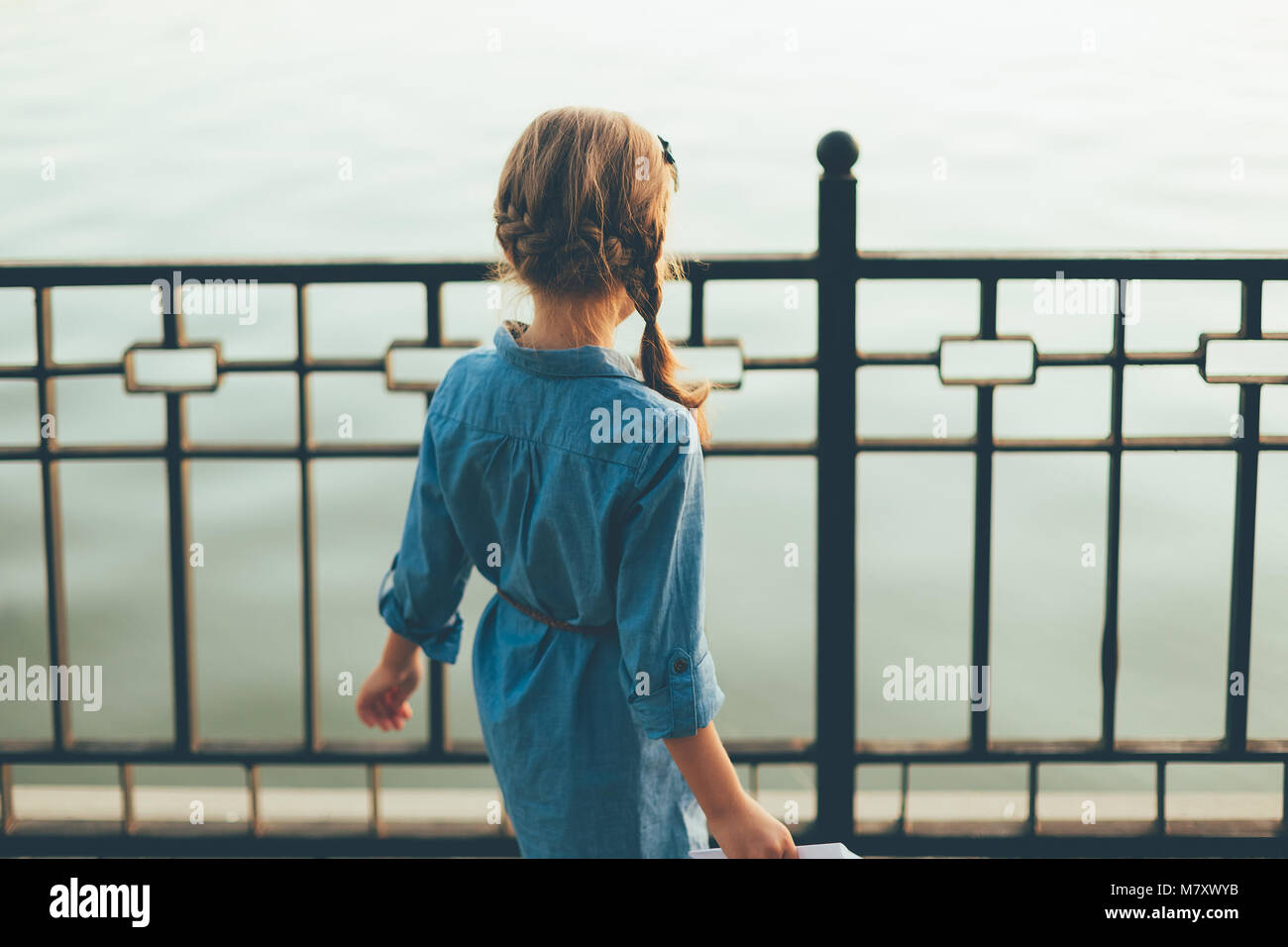 Close-up back view of child playing in the park looking yo lake in ...