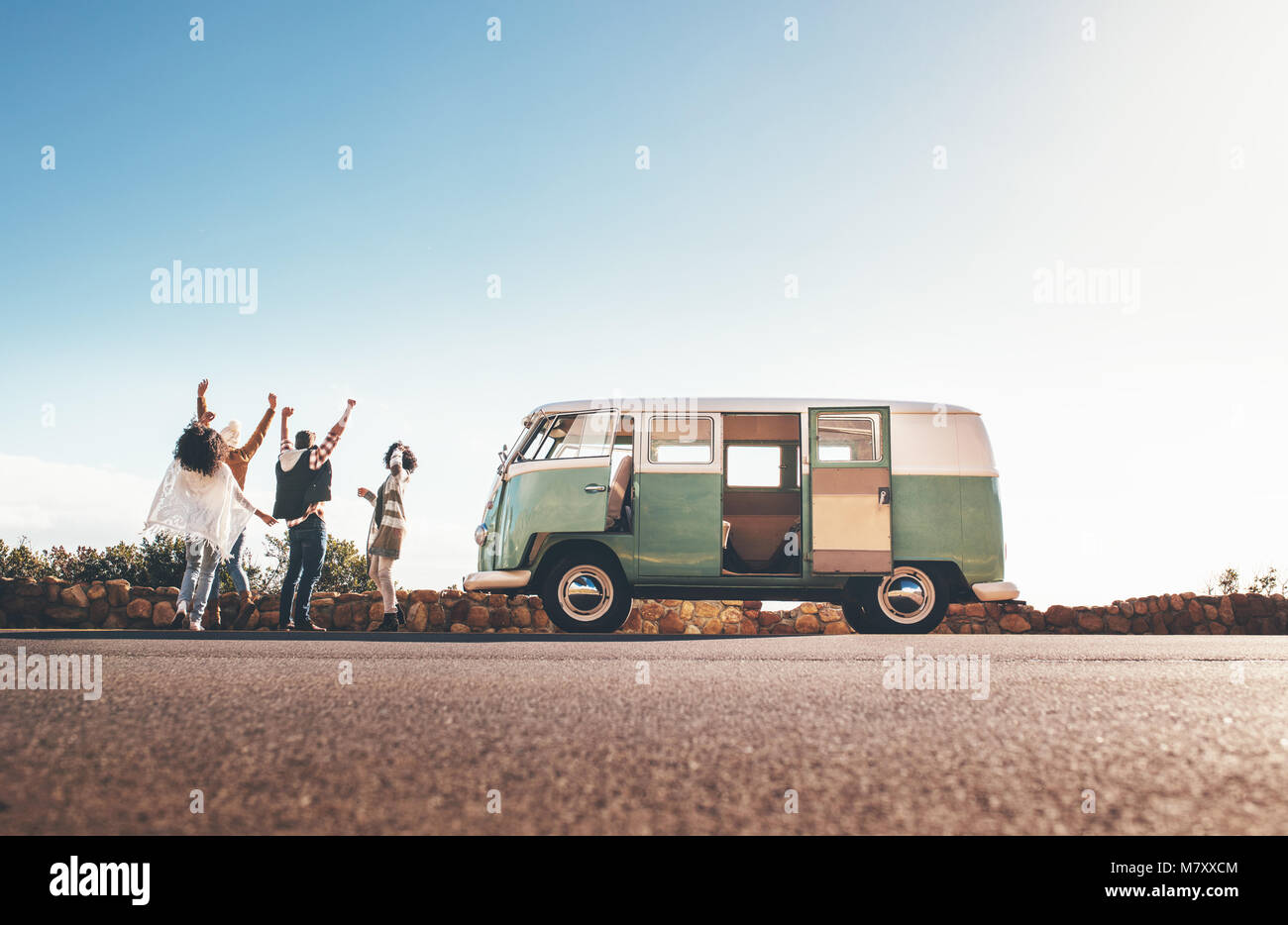 Friends dancing outdoors and having fun on roadtrip. Old minivan on ...