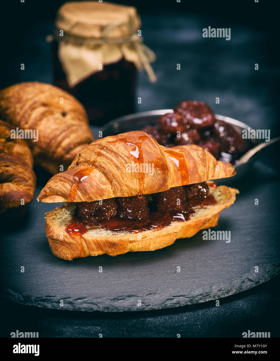 baked croissant with strawberry jam on a black background, vintage ...