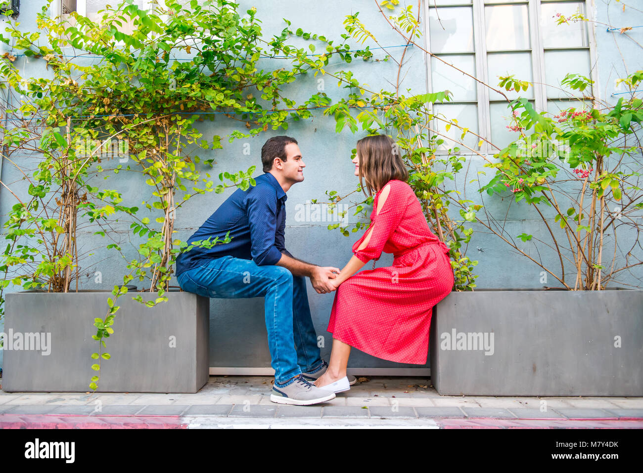 Profiles of young couple sitting opposite each other on the flower pots ...