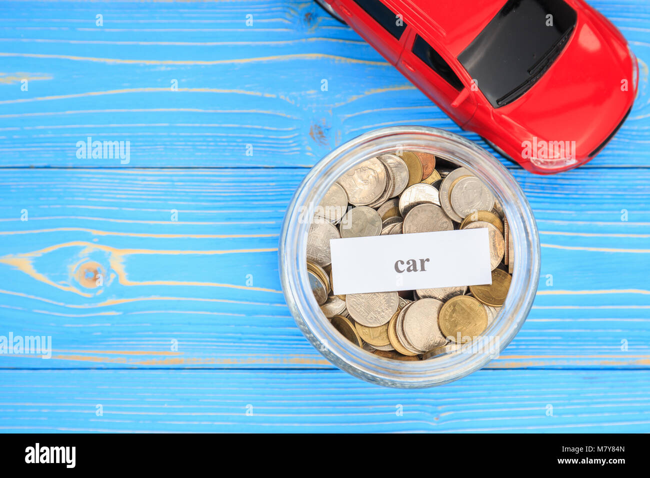 Top view coin in clear jar with paper note on blue wooden plank ...