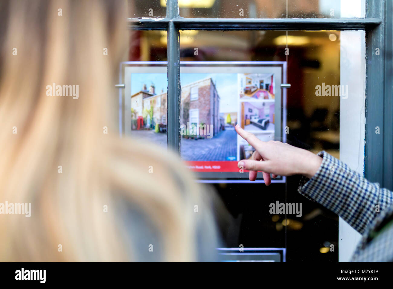 Couple looking and pointing at a property advert in the window of an ...