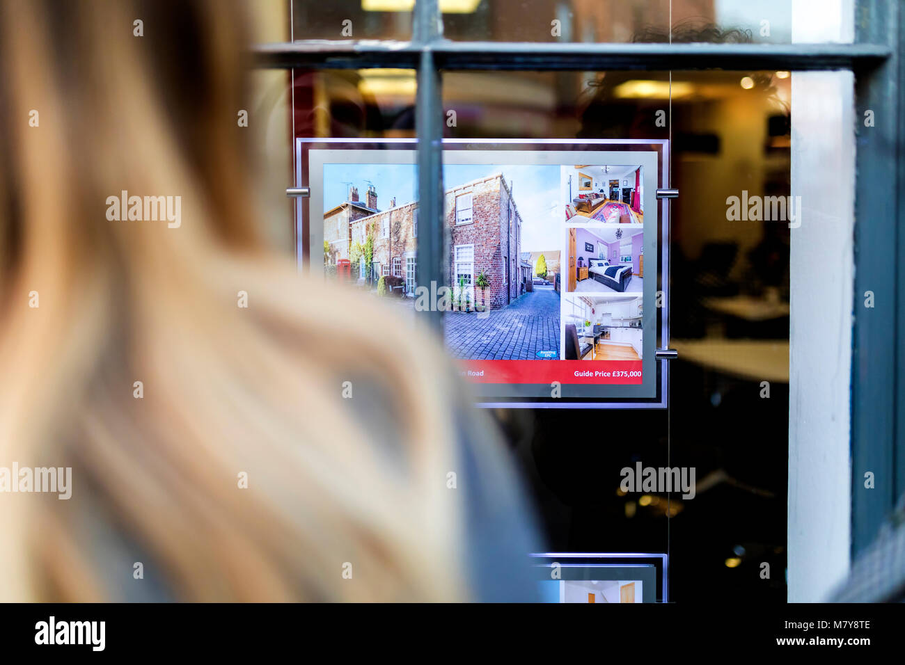 Woman looking at a property advert in the window of an estate agents or ...