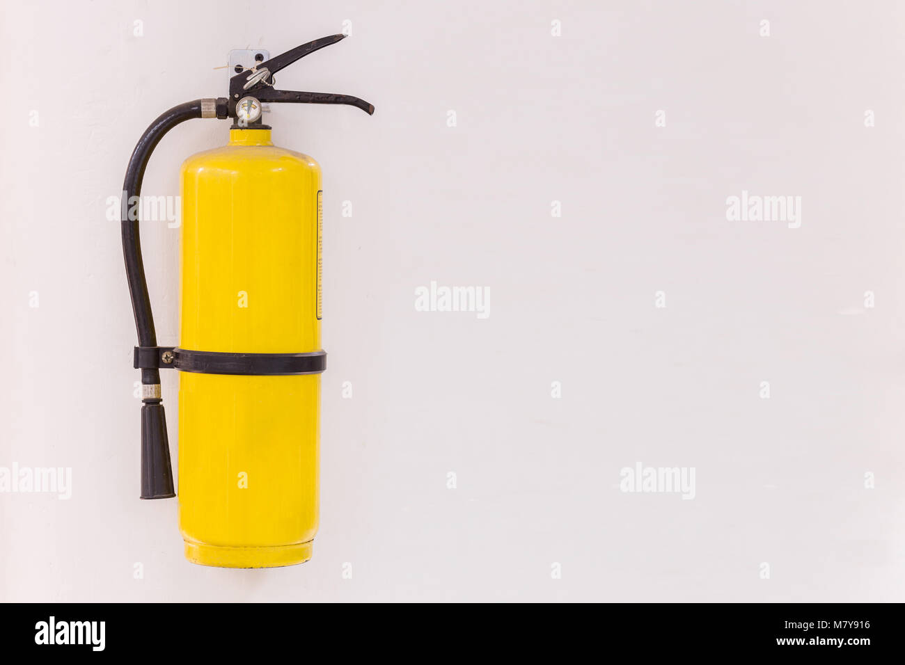 Old yellow fire extinguisher tank setting on the white wall. And empty ...