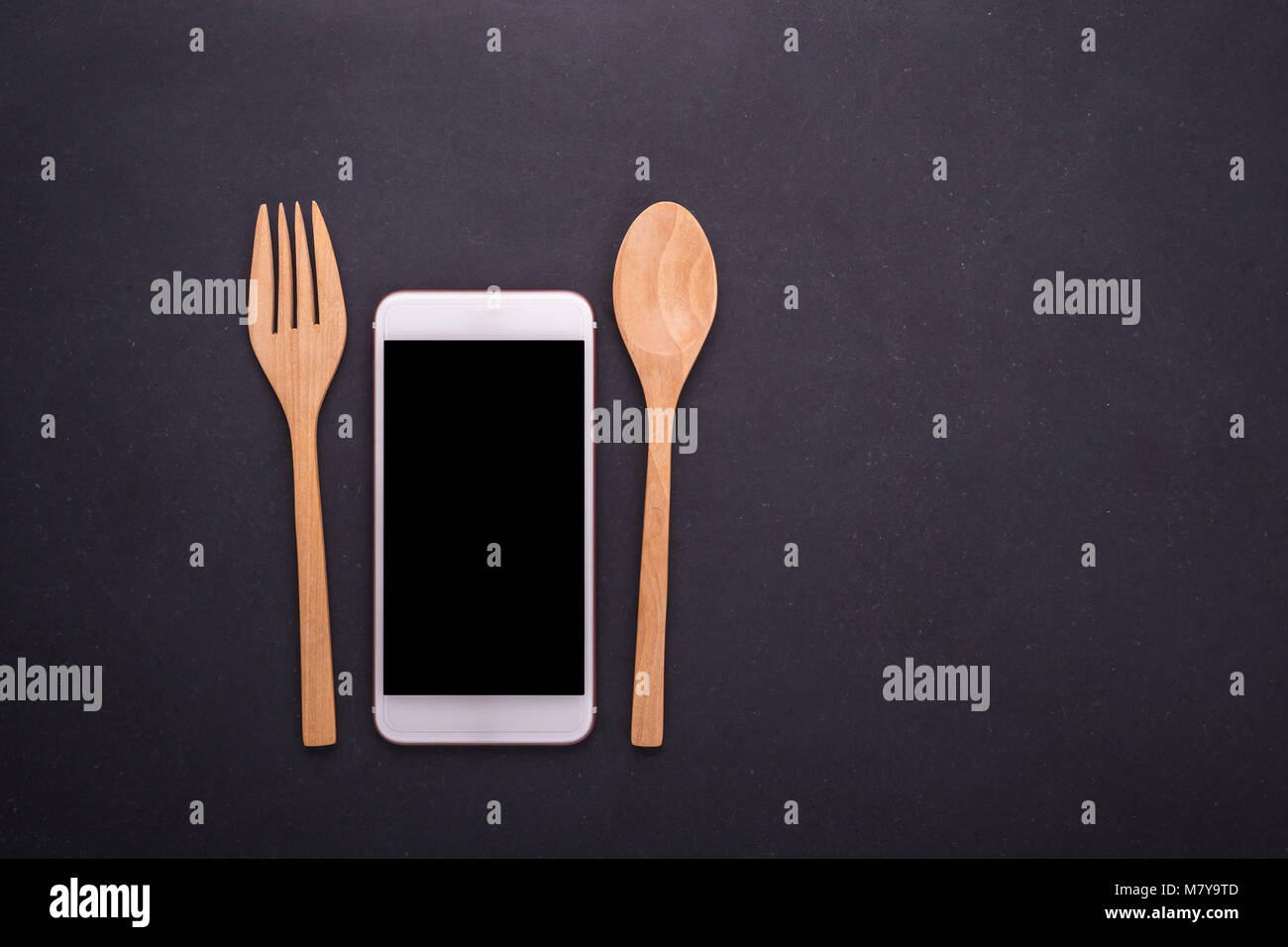 Top view smartphone, spoon and fork on black stone table background ...