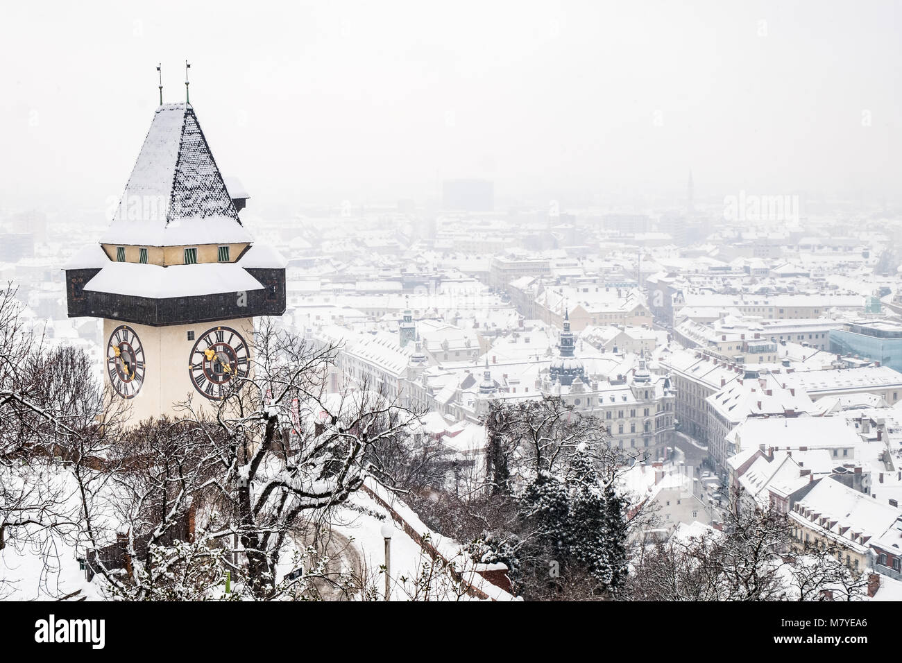 Snow covered Uhrturm clocktower landmark on hill Schlossberg with ...