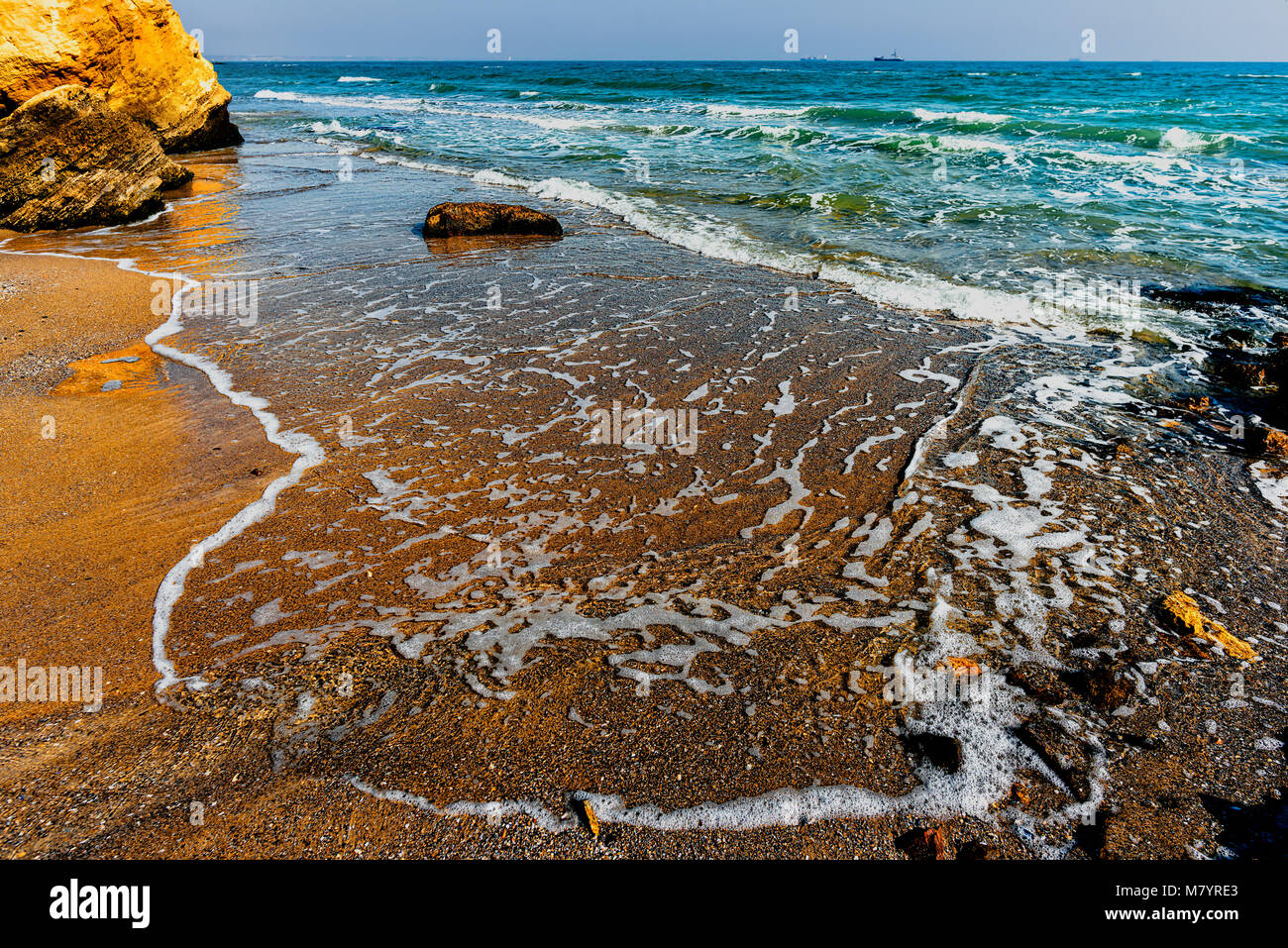 sandy ocean shore with yellow rocks, sea waves with white foam, ships ...