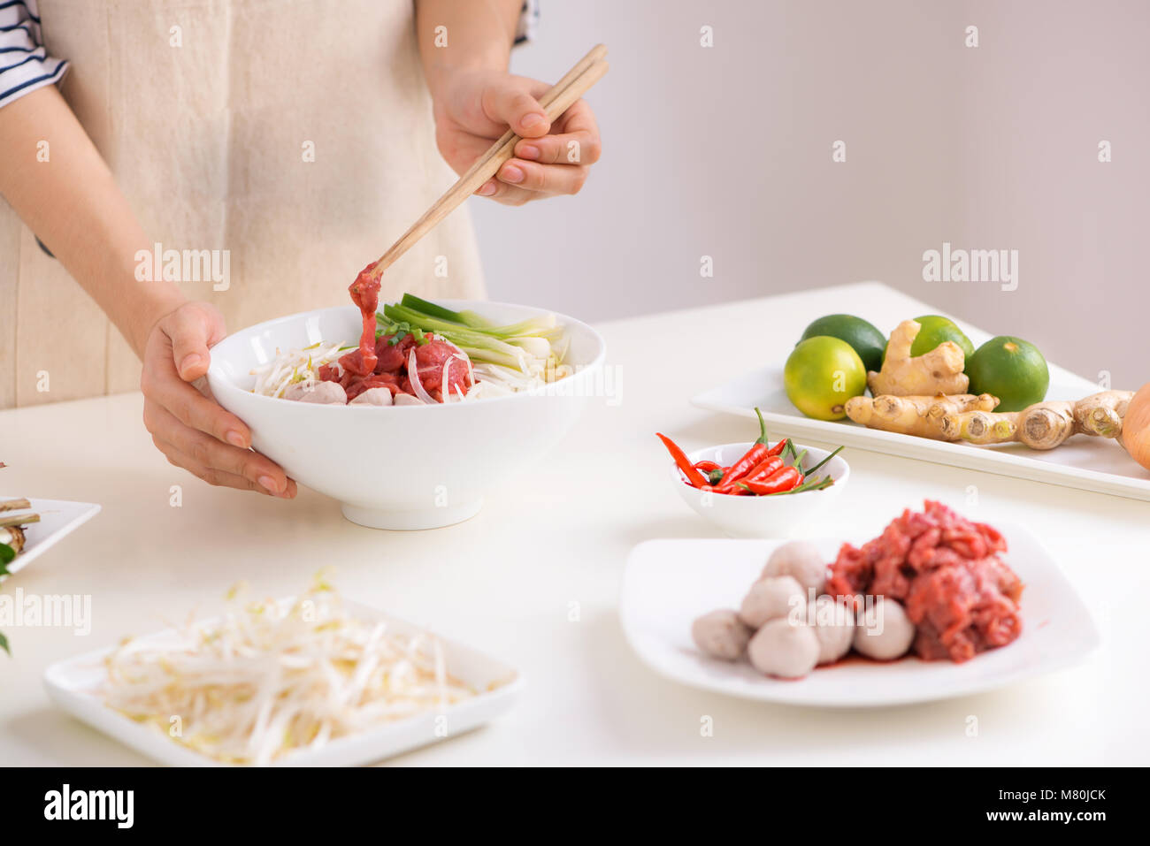 Female chef prepare traditional Vietnamese soup Pho bo with herbs, meat ...