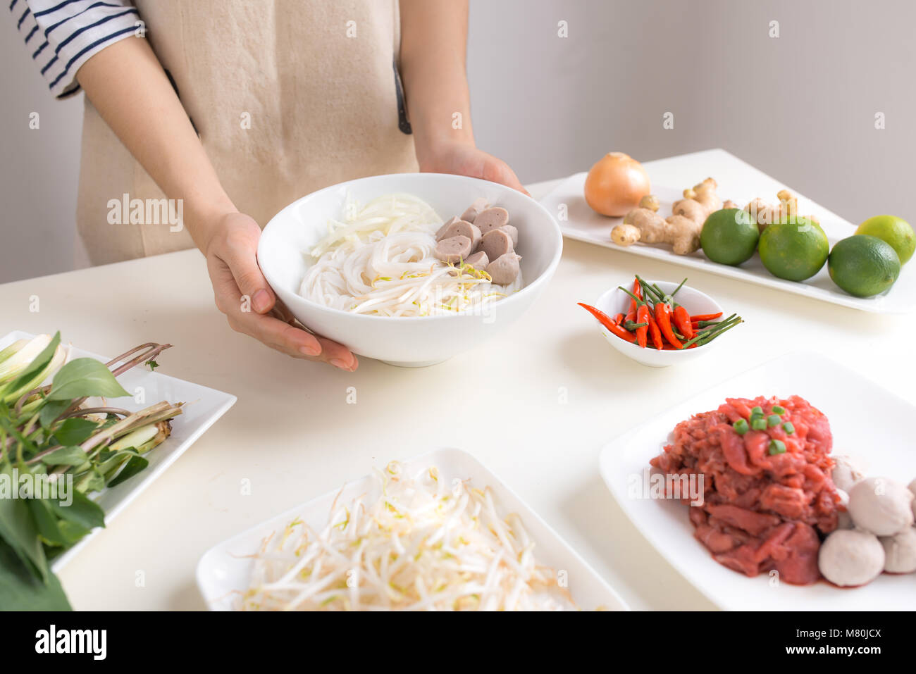 Female chef prepare traditional Vietnamese soup Pho bo with herbs, meat ...