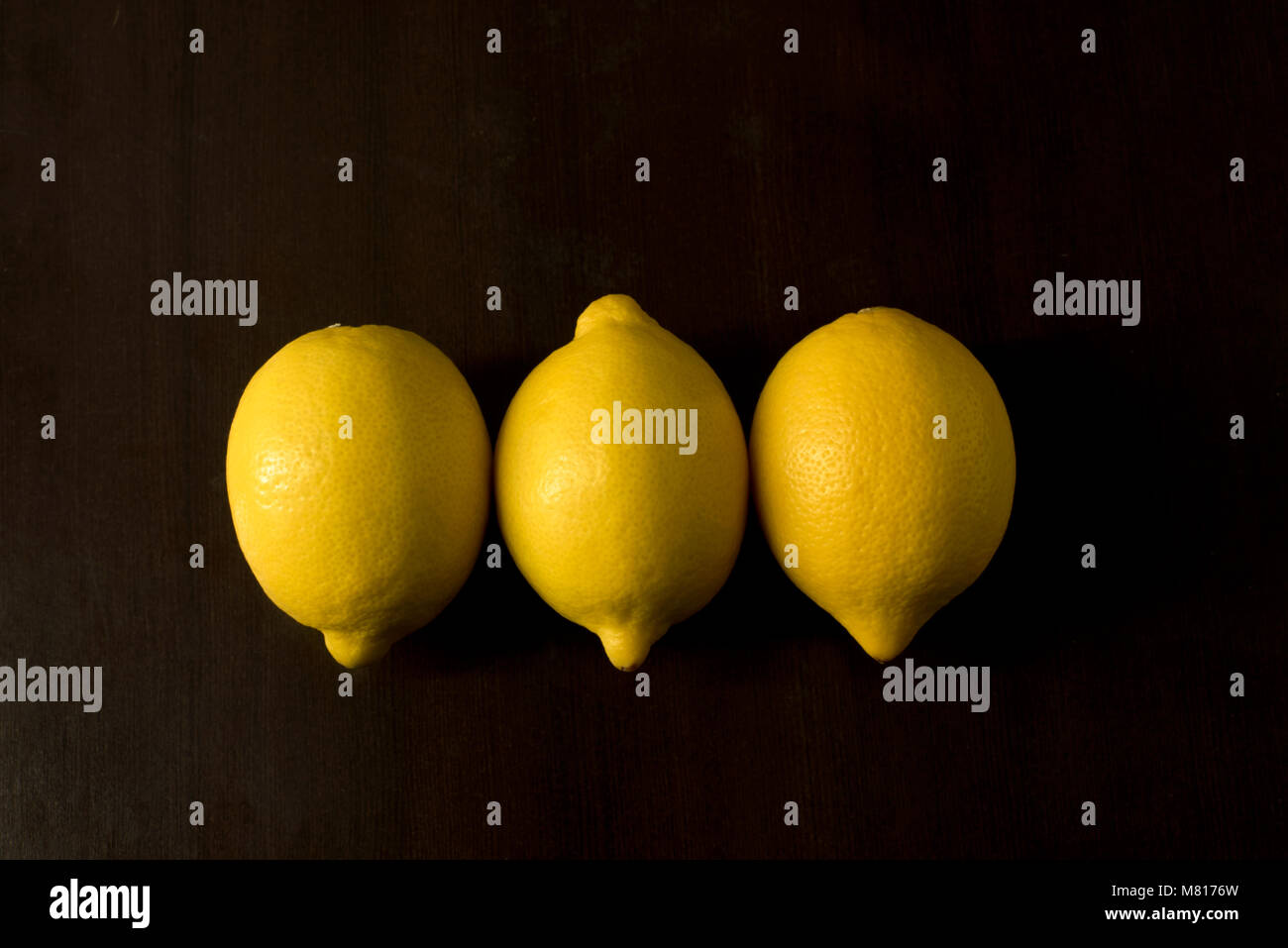 Group of three lemons in a row- view from above on dark background ...